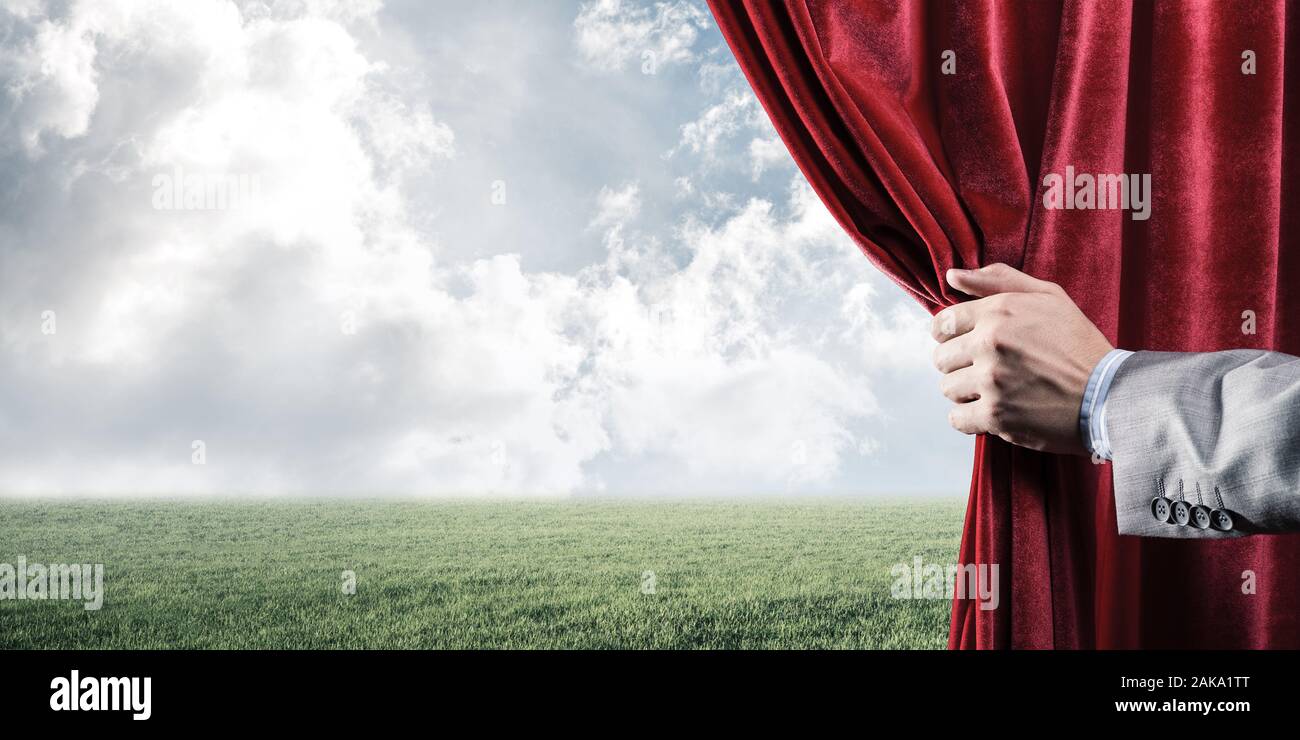 Green meadow behind red curtain and hand holding it Stock Photo - Alamy