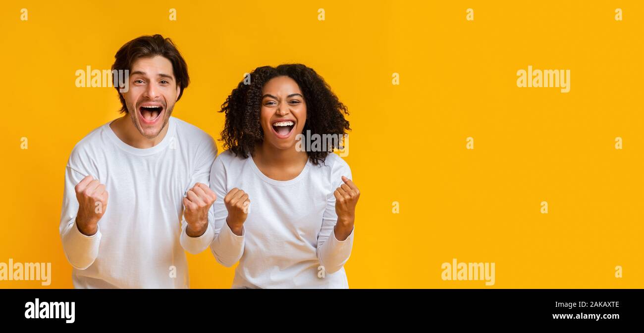Joyful multiracial couple rejoicing success, raising fists with ...