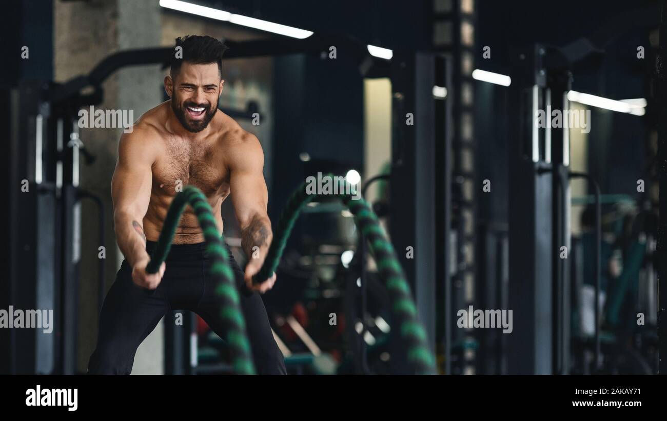 Waves of force. Muscular bodybuilder training with battle rope at gym ...