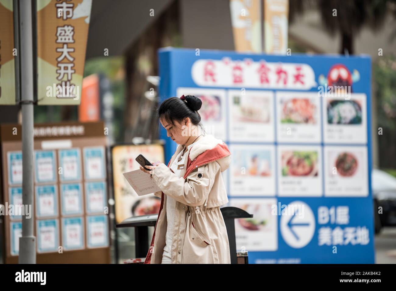 A beautiful young Chinese lady using her cell phones while walking into ...