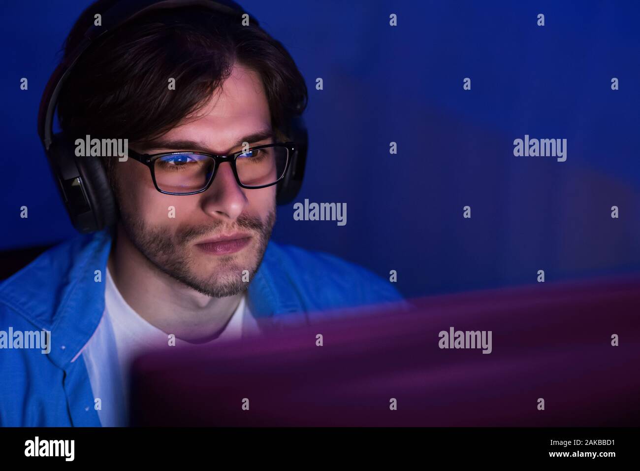 Pro gamer playing video game wearing headset and illuminated by screen ...