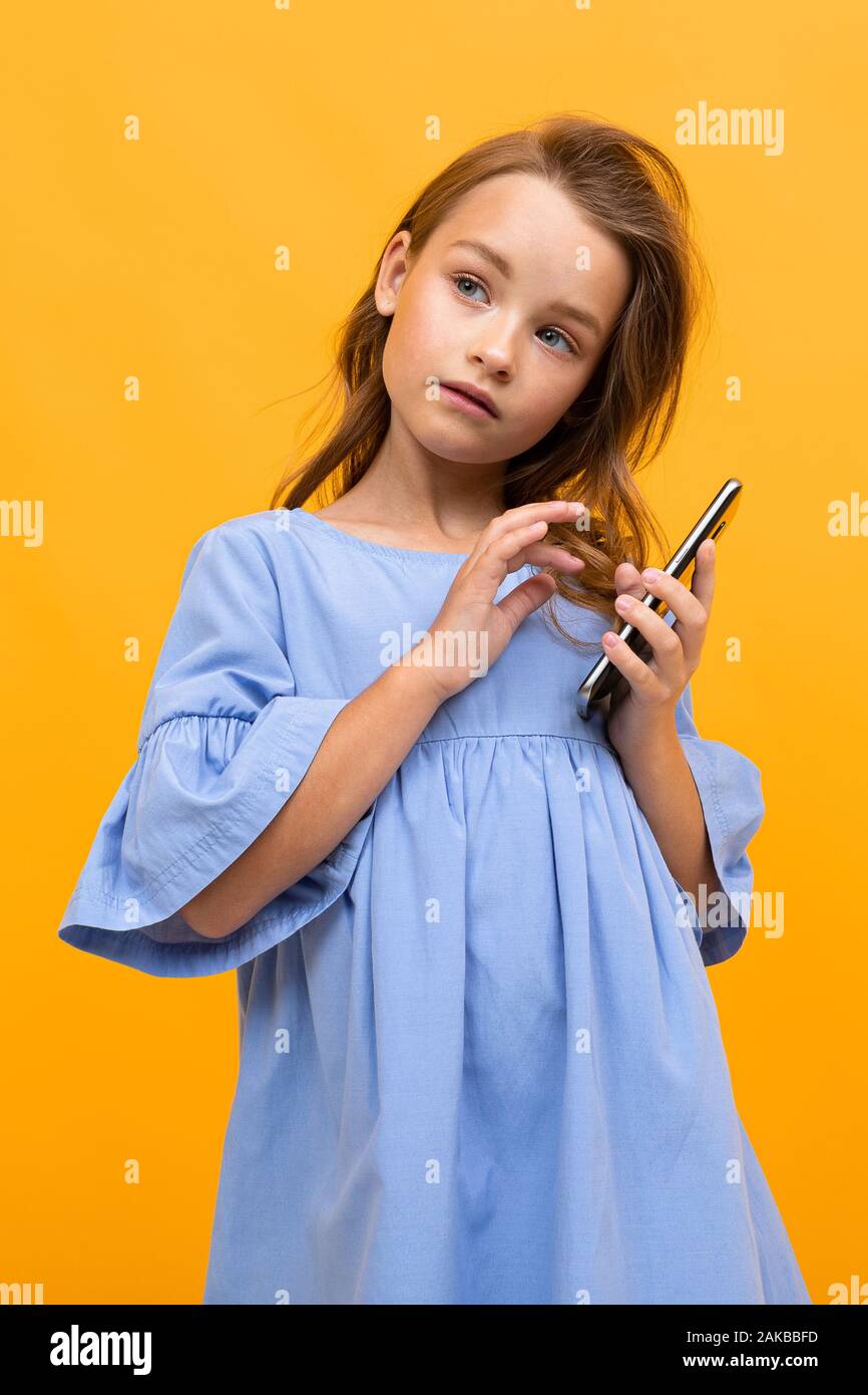 cute smiling girl in a blue dress is waiting for an answer to a phone ...