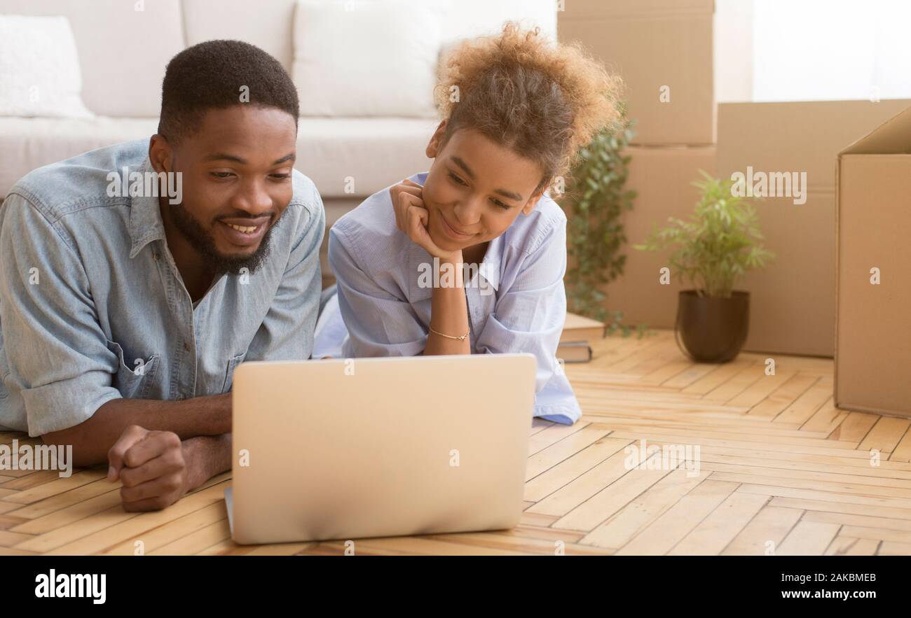 Joyful Afro Spouses Using Laptop Lying On Floor Relaxing In New House ...