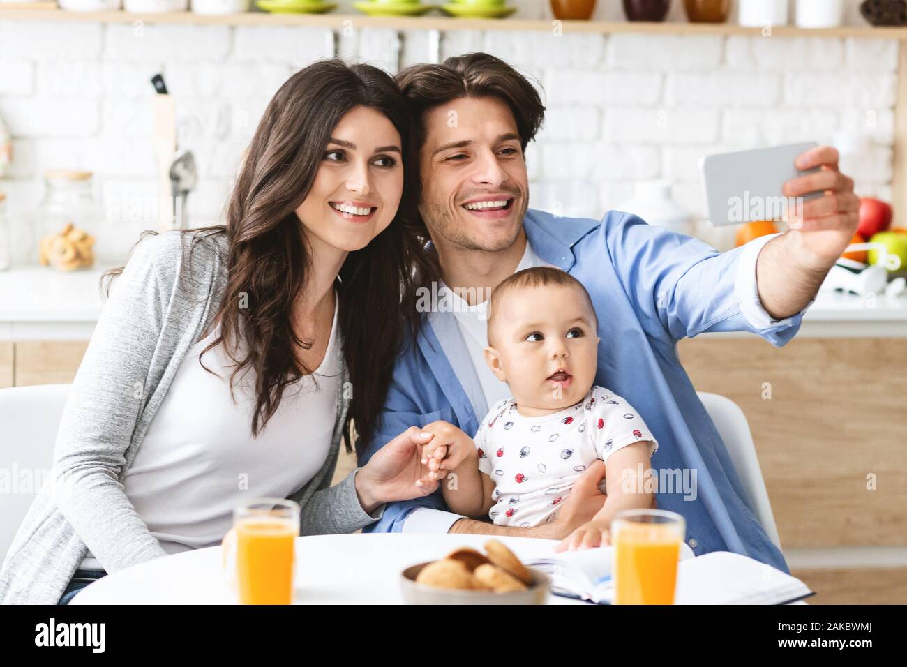 Social media content. Happy parents taking selfie with baby at kitchen ...