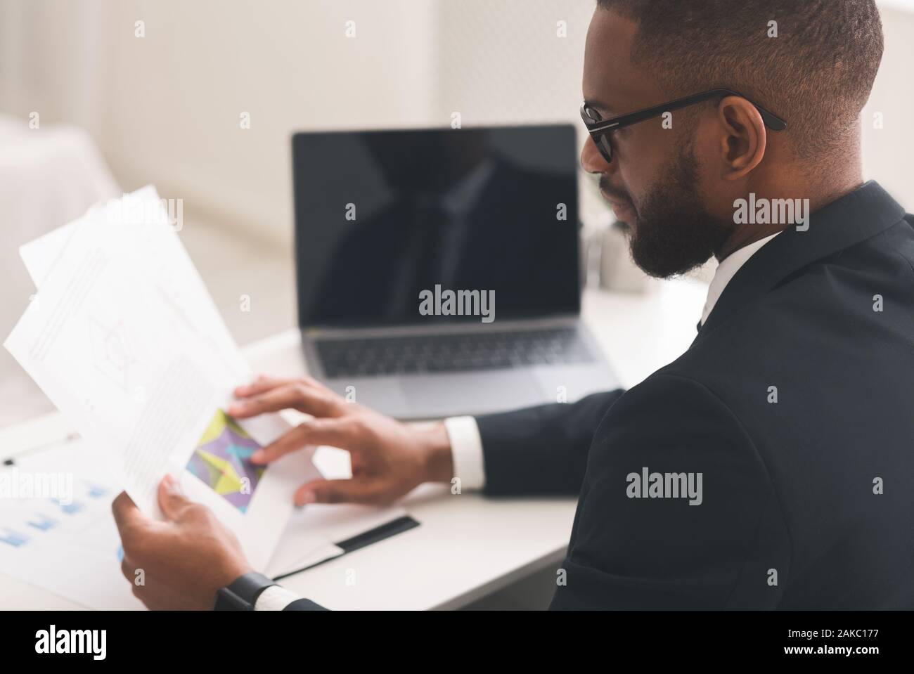 Young black manager in glasses sitting in front of laptop and reading ...