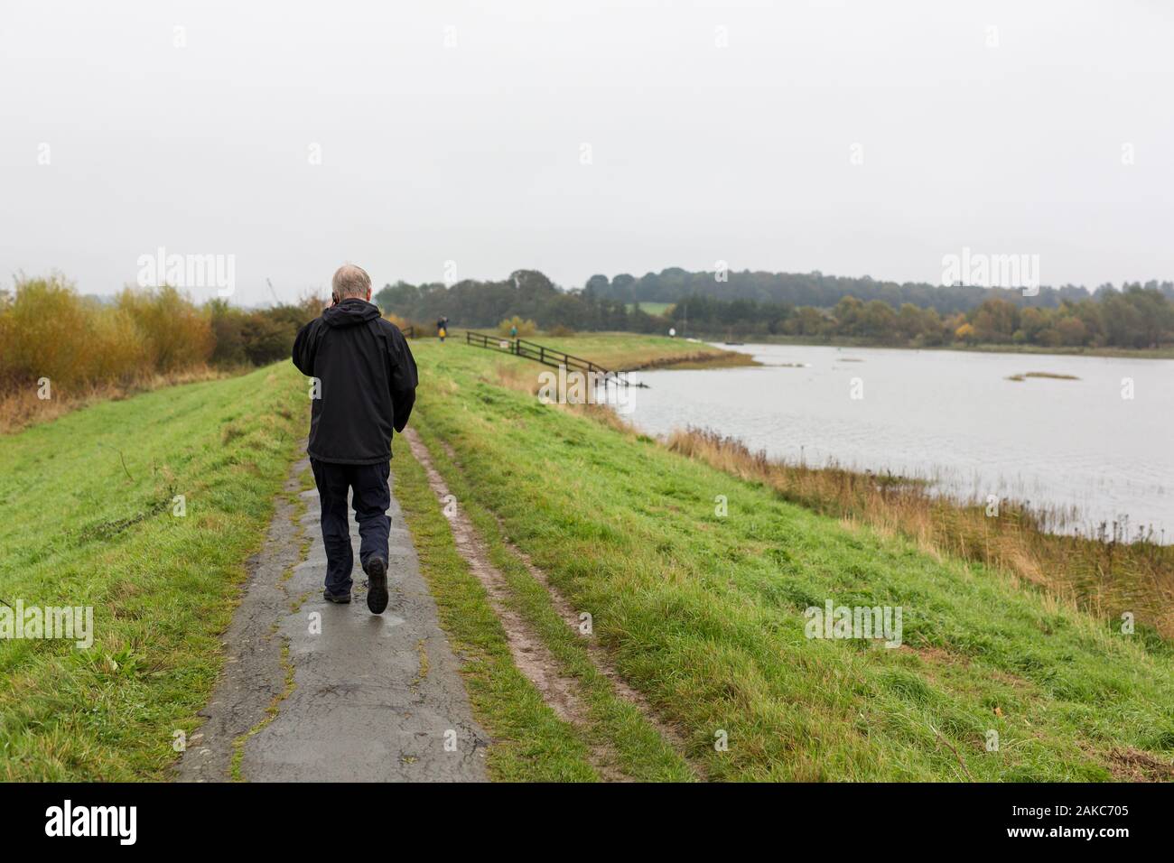 A middle aged man walking along a river path while talking on his ...
