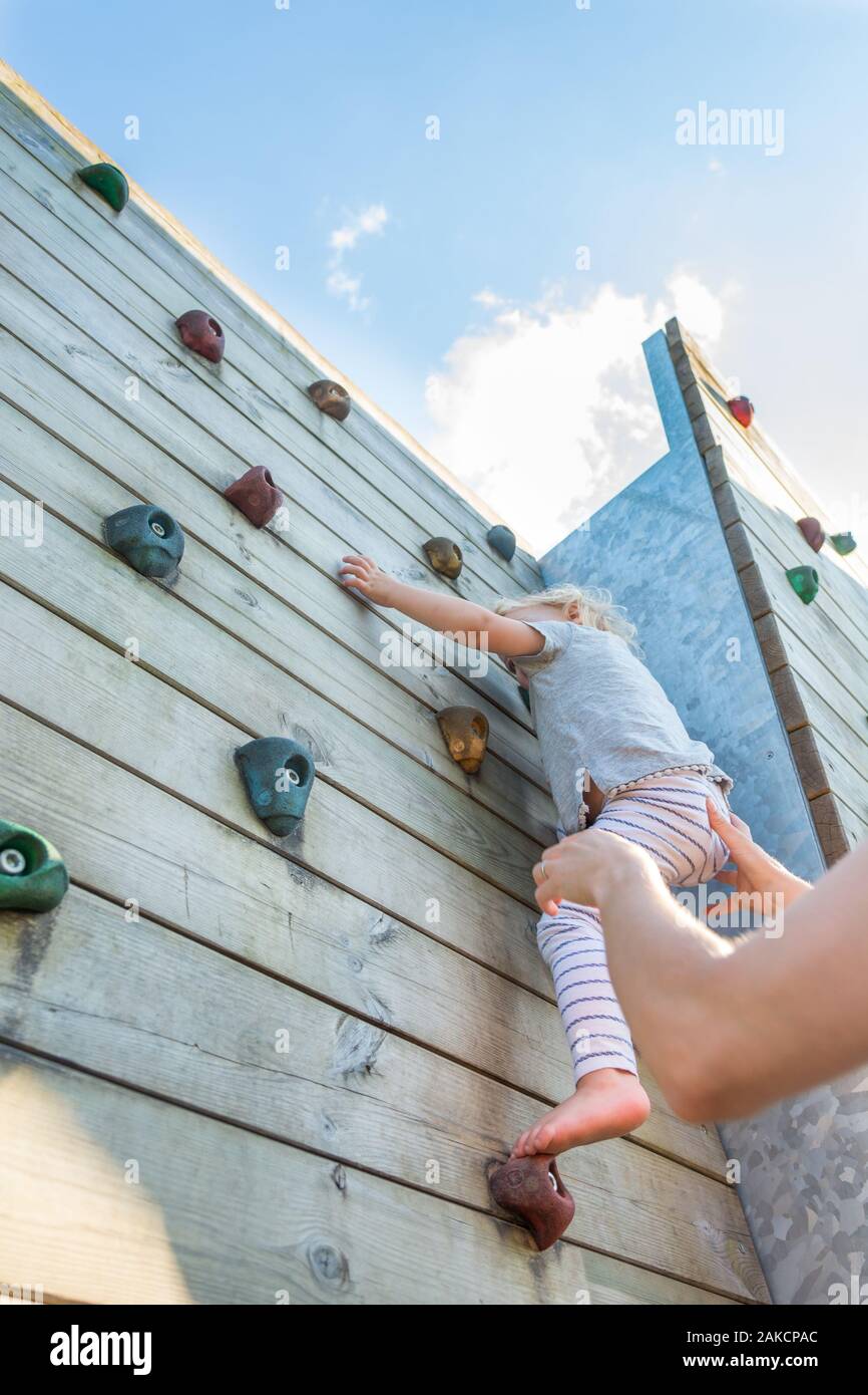 Mother supporting her cute blonde girl climbing plastic boulder holds ...
