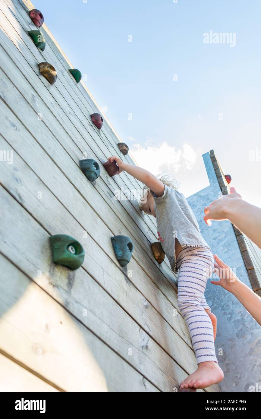Mother supporting her cute blonde girl climbing plastic boulder holds ...