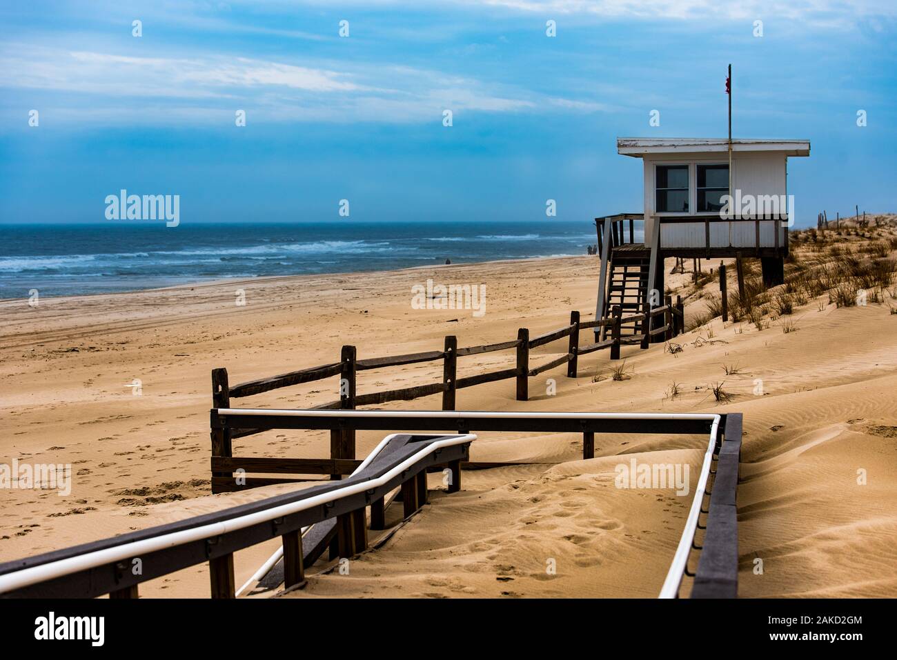 A life guard hut on a sandy beach with waves and a cloudy blue sky ...