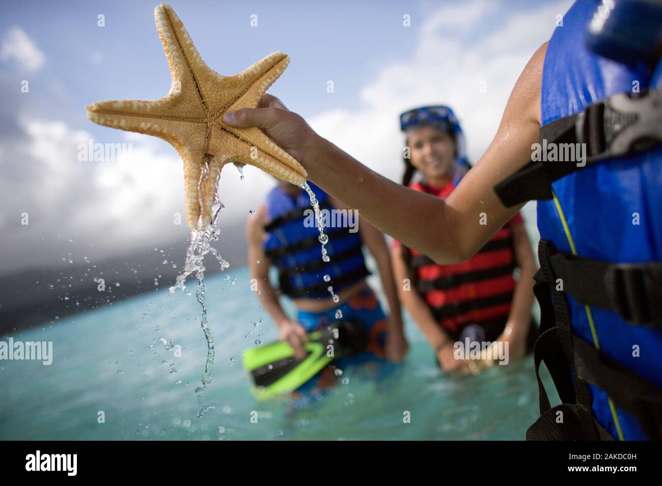 Starfish held up by group of children standing waist deep in the ocean ...
