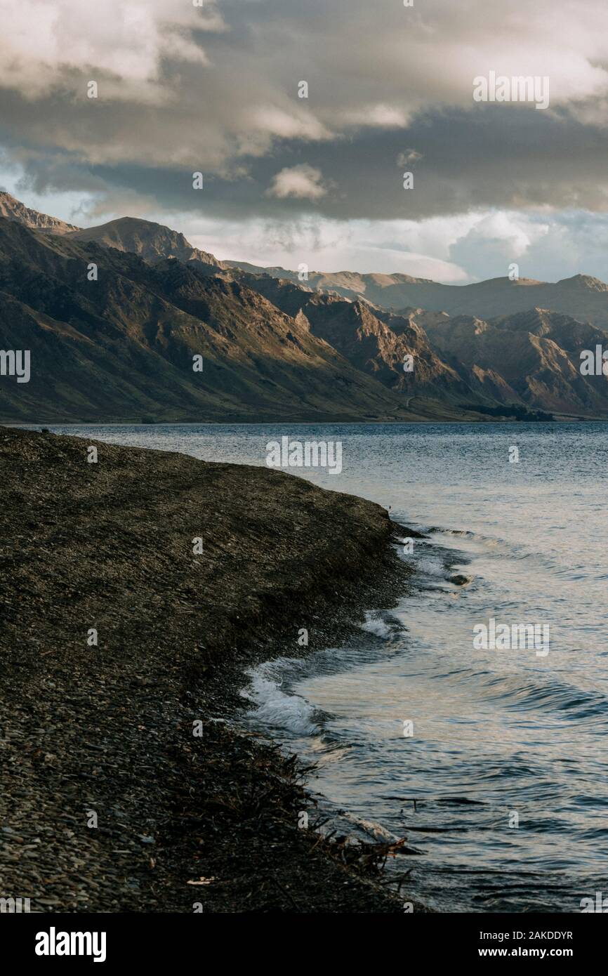 view of sunset over jagged mountains from beach next to Lake Hawea ...