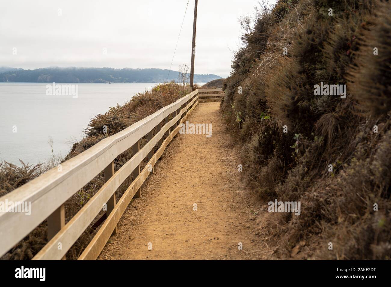 Dirt walking path with white rail overlooking cliff a body of water ...
