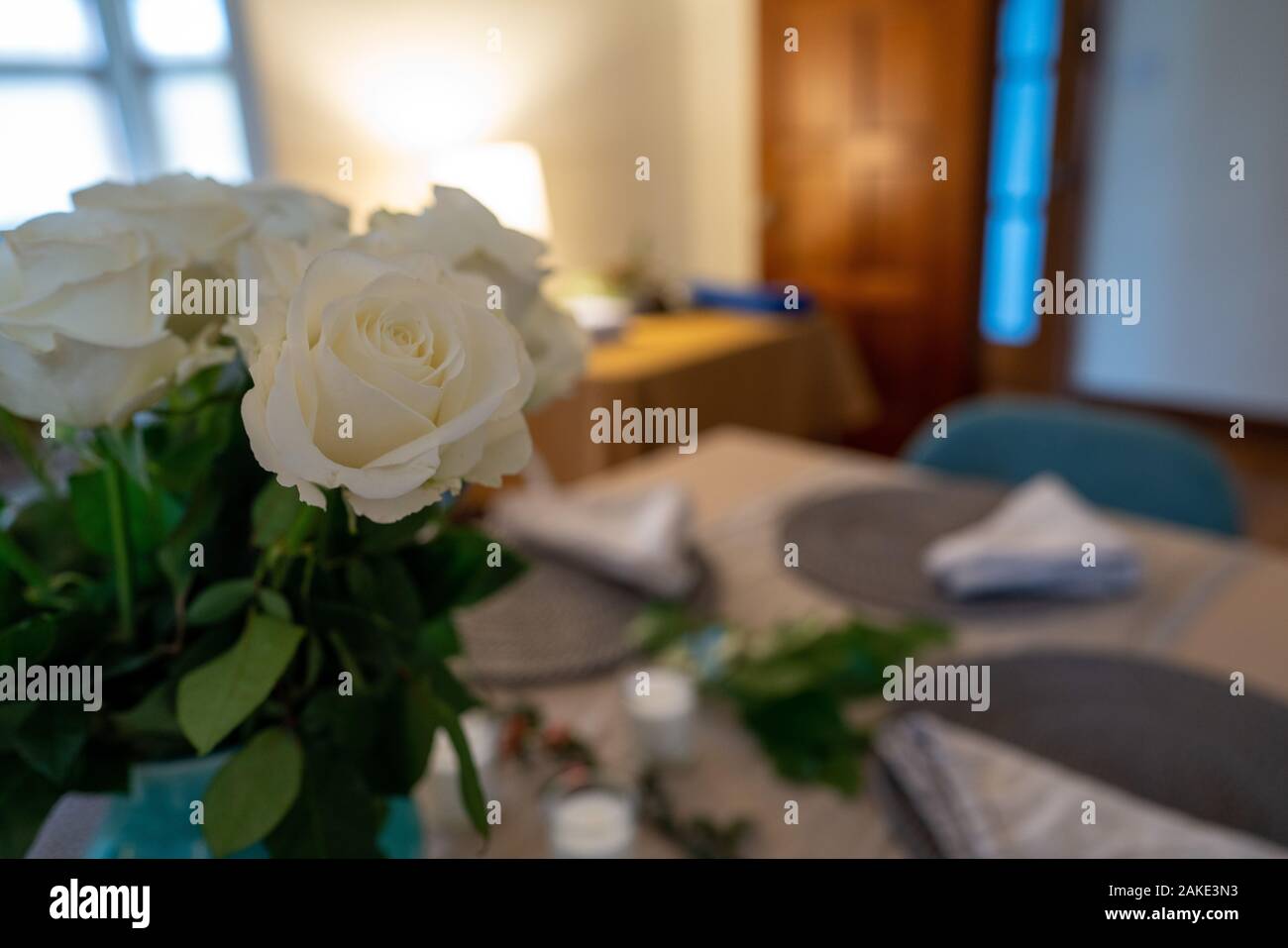 White roses in a case on a simple table setting in home living room ...