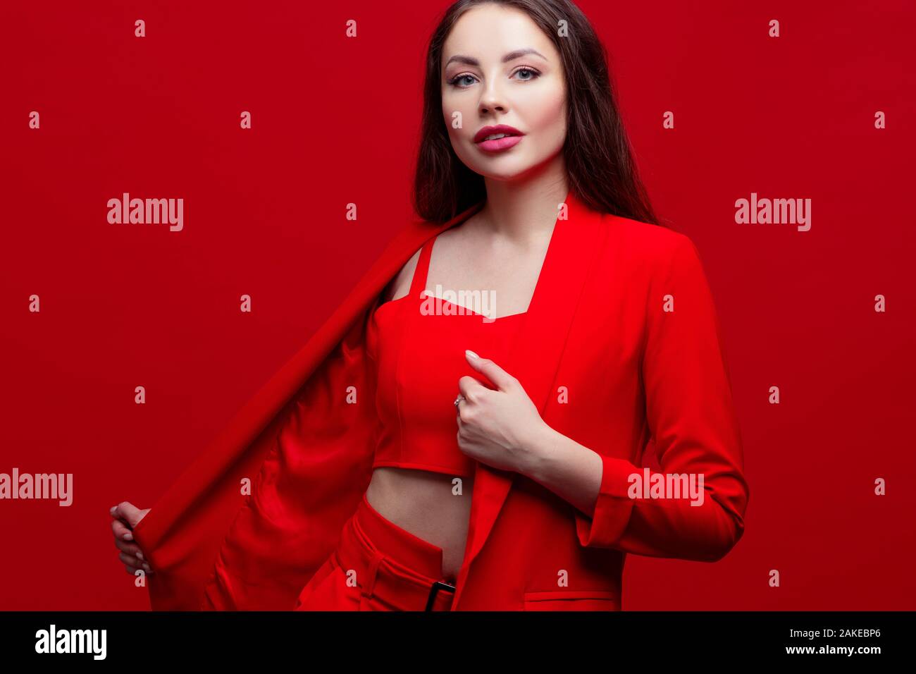 Stylish young woman in a red suit on a red background. One-color image ...