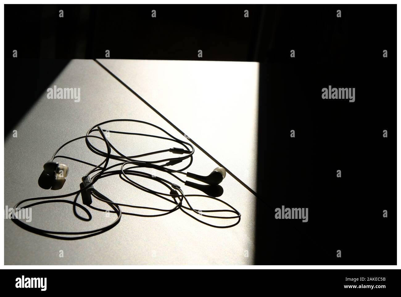earphones lying in light and shadow on white table Stock Photo - Alamy