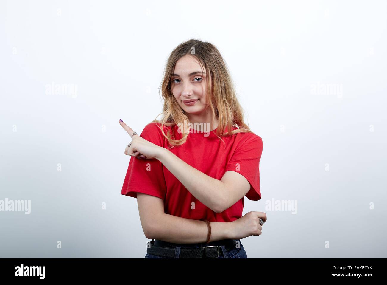 Cheerful young woman keeping hand on stomach, pointing finger behind ...