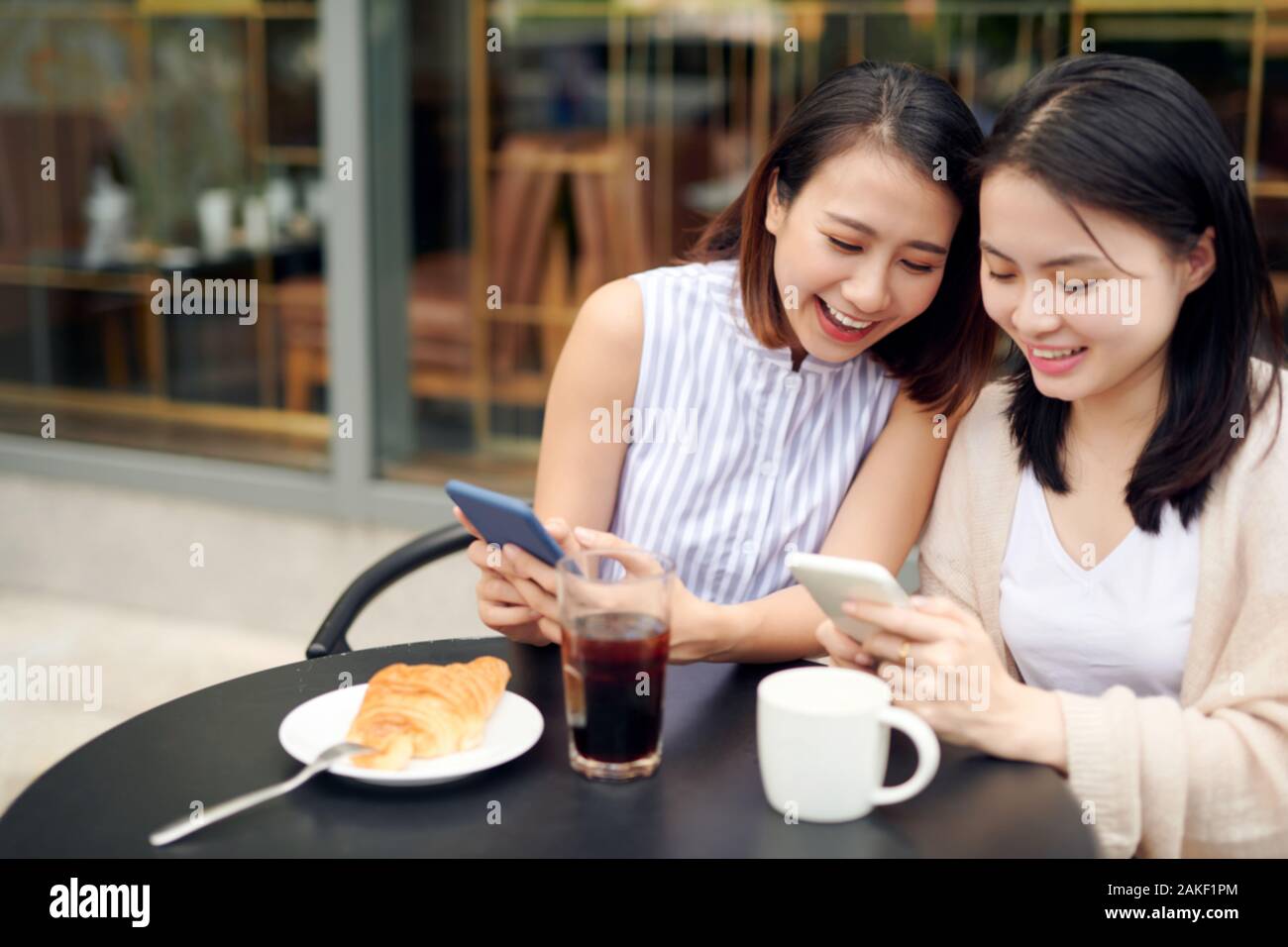 Happy girls using mobile in cafeteria Stock Photo - Alamy