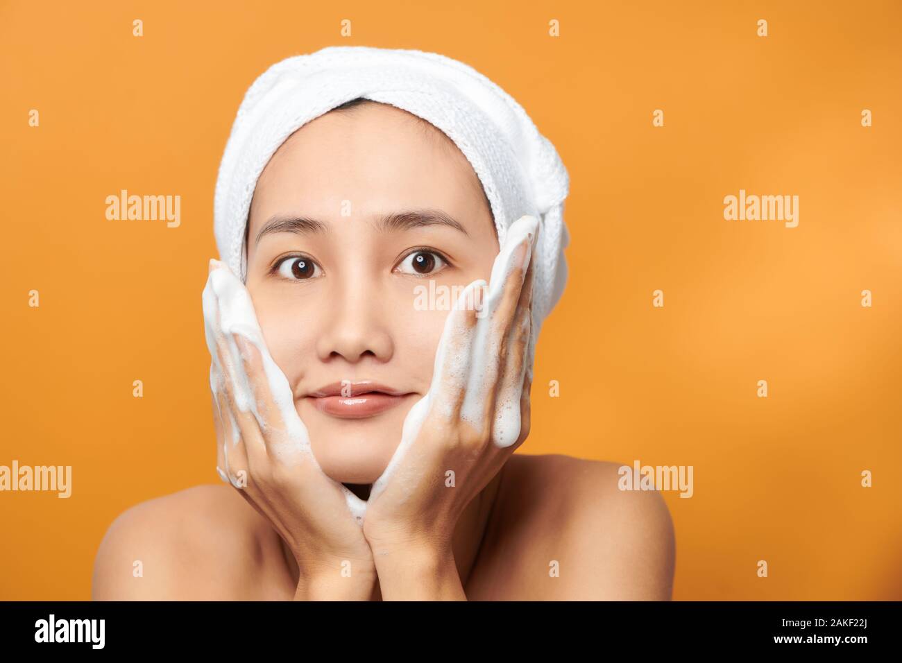 Beautiful Model Applying Cosmetic Cream Treatment On Her Face On Orange