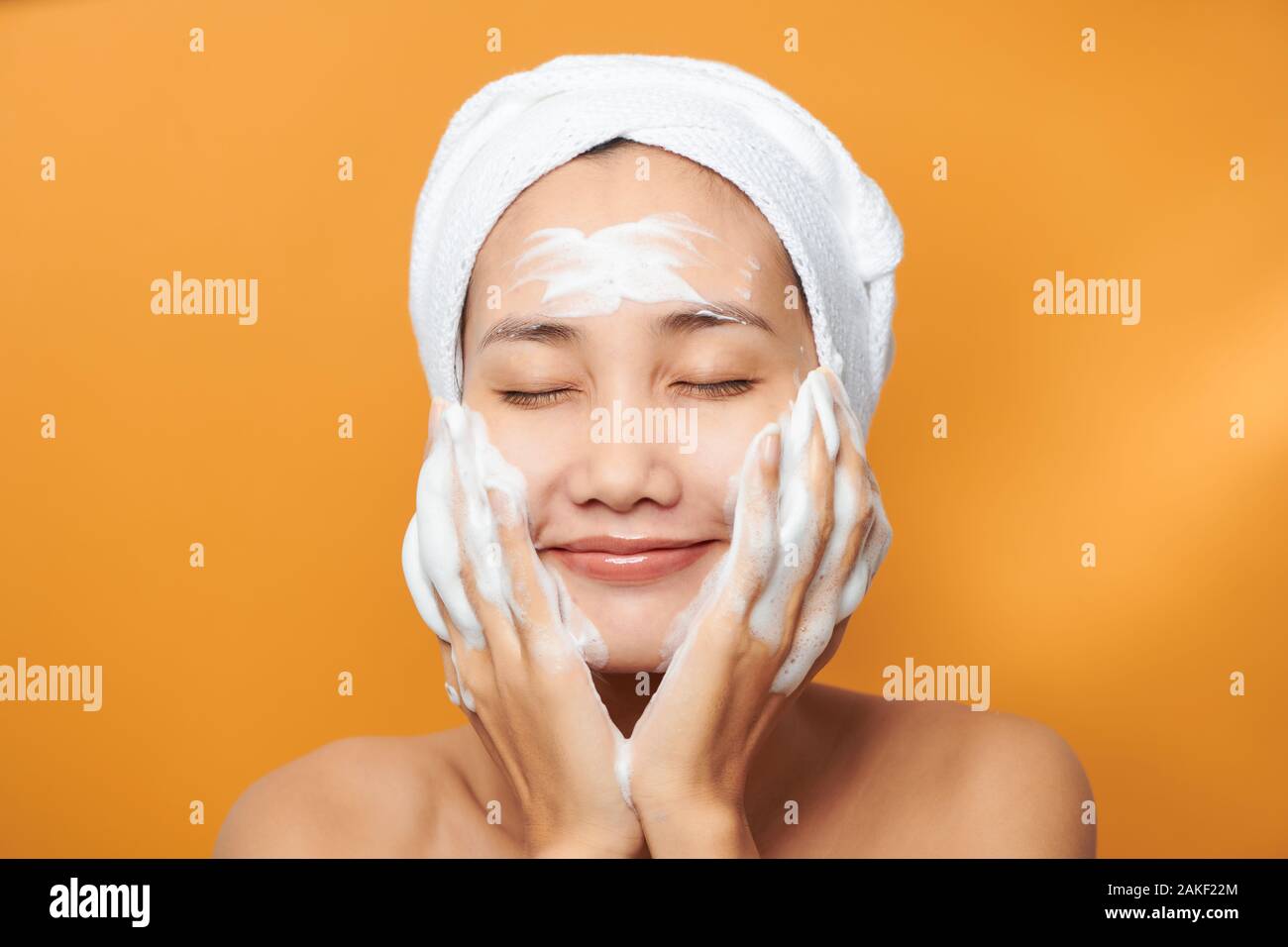 Beautiful model applying cosmetic cream treatment on her face on orange ...