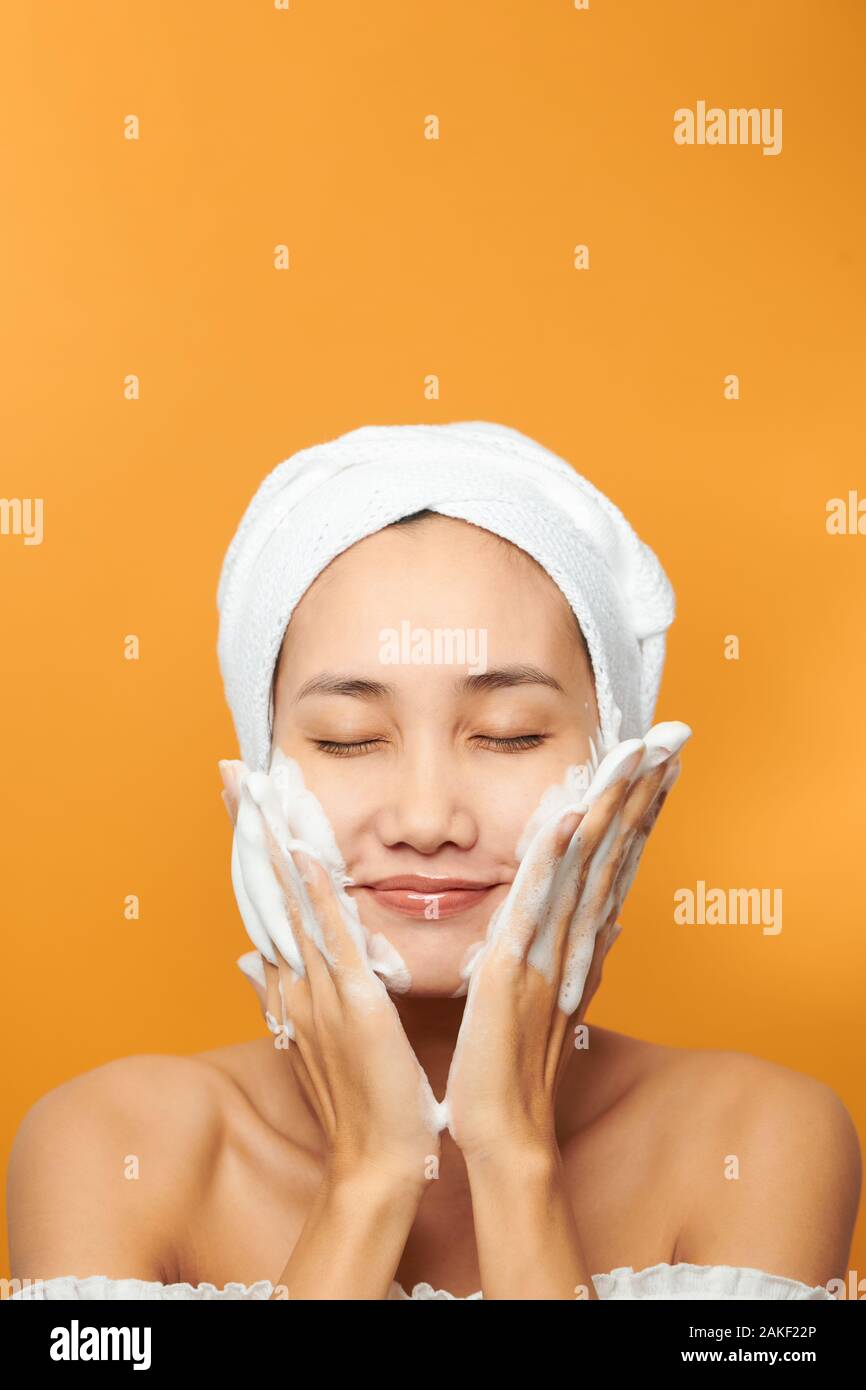 Beautiful Model Applying Cosmetic Cream Treatment On Her Face On Orange