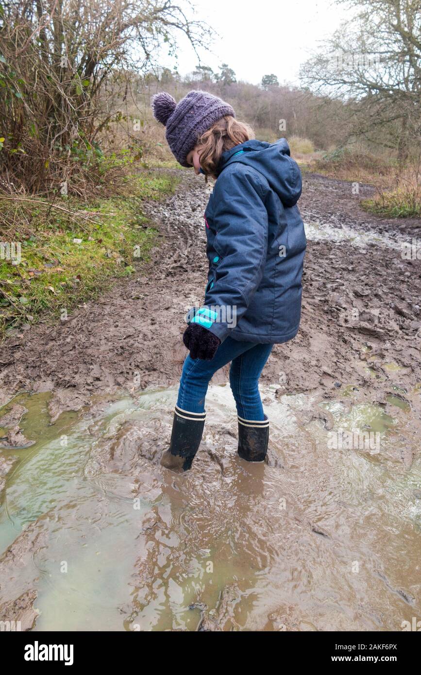 Young girl age 7, wearing Wellington boots, enjoys standing and playing ...