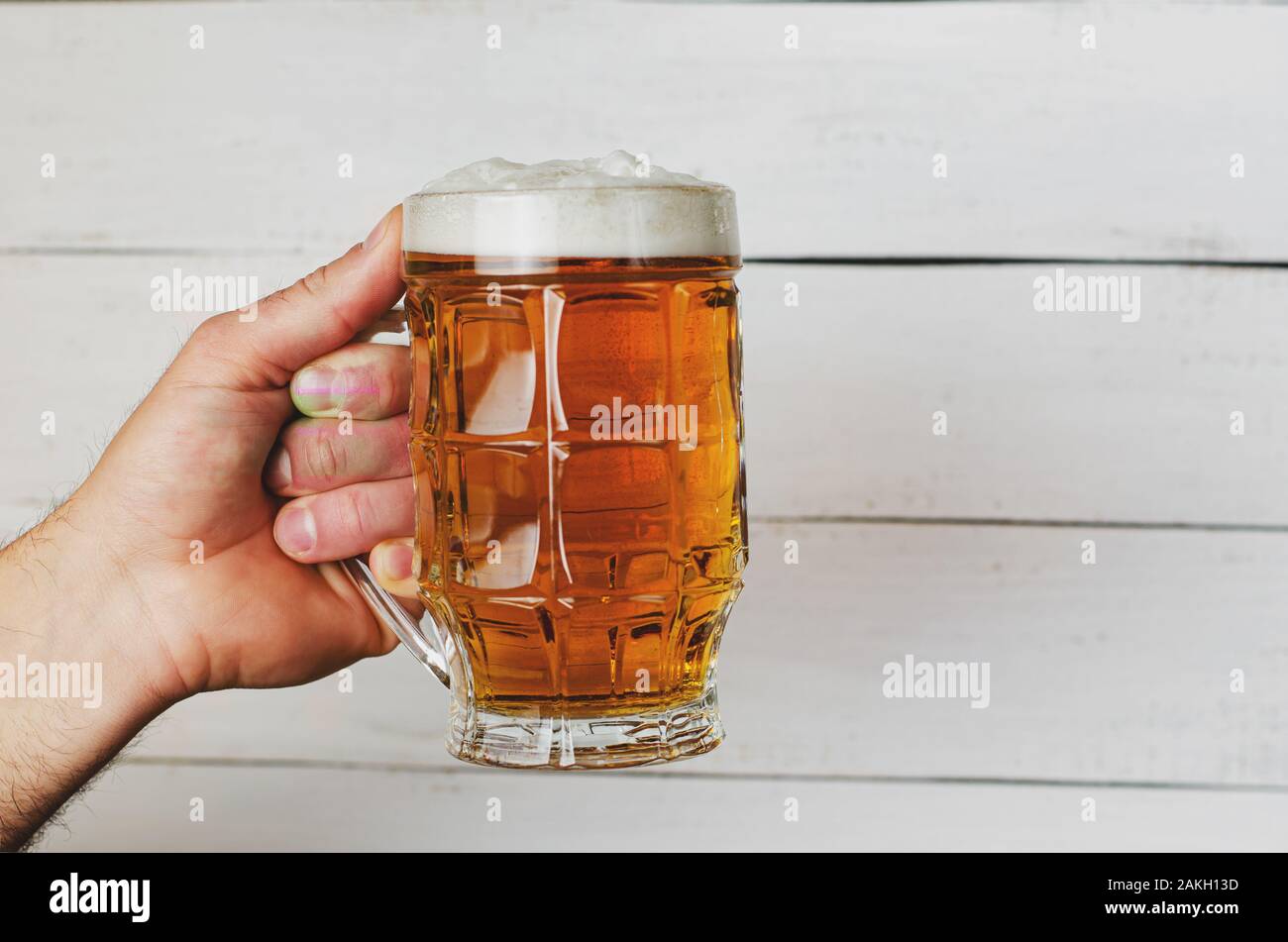 Male hand holding a full beer mug on white wooden background. Toned ...