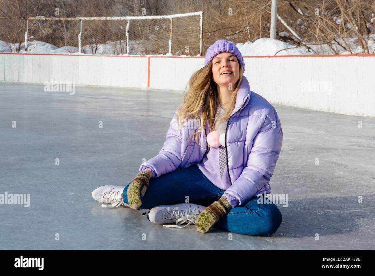 Lovely young woman sitting on the ice rink with ice skates on feet ...