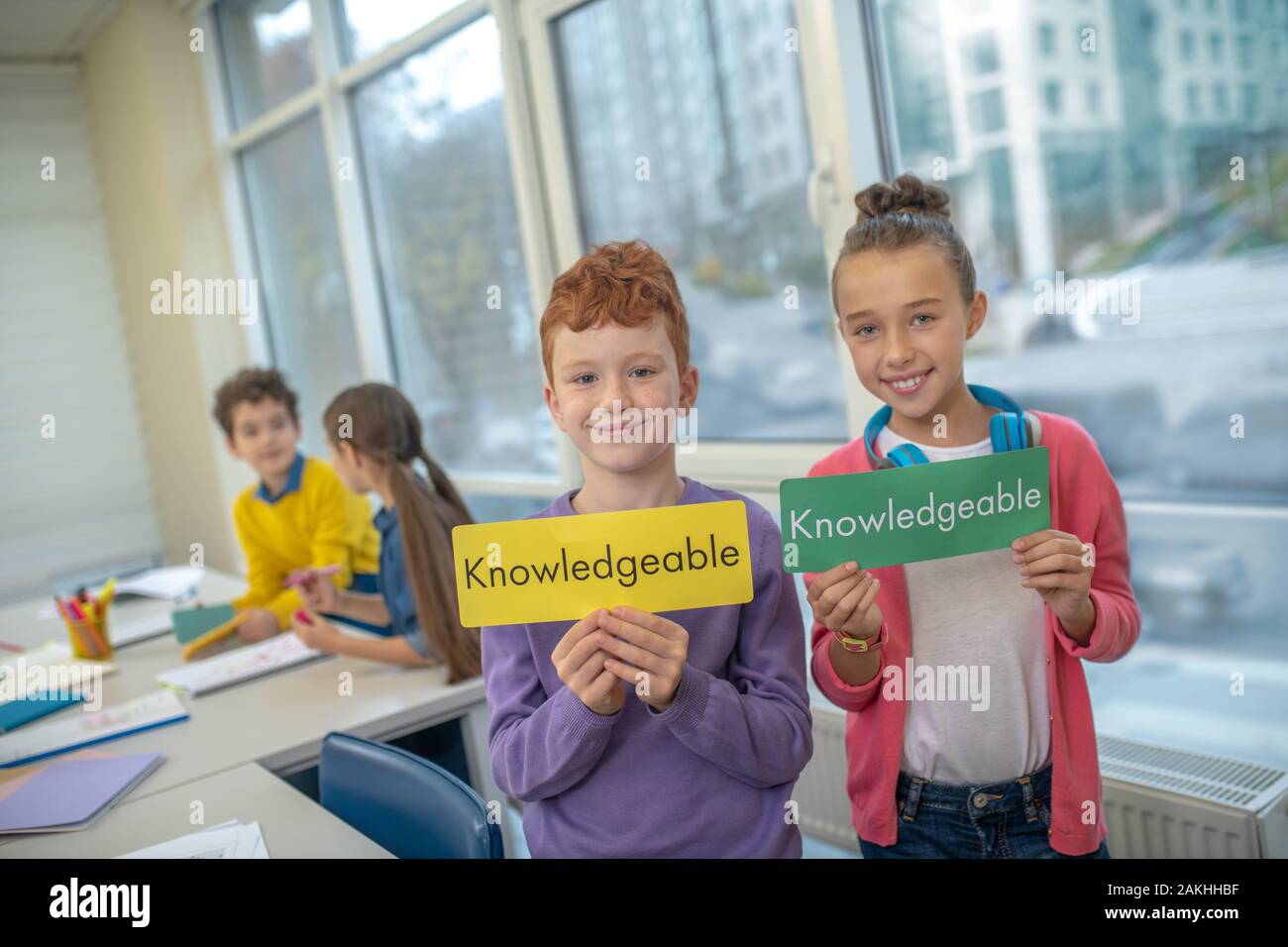 Two smiling kids holding the word knowledgeable Stock Photo - Alamy