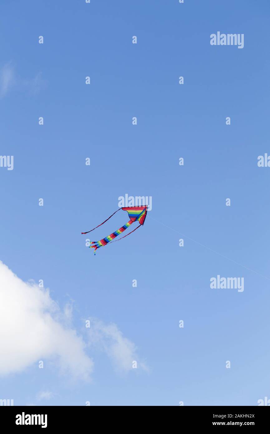 A multicoloured kite with streamers flying high in a blue sky with ...