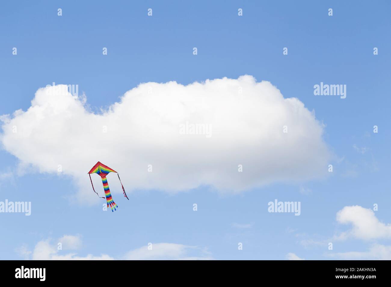 A multicoloured kite with streamers flying high in a blue sky with ...
