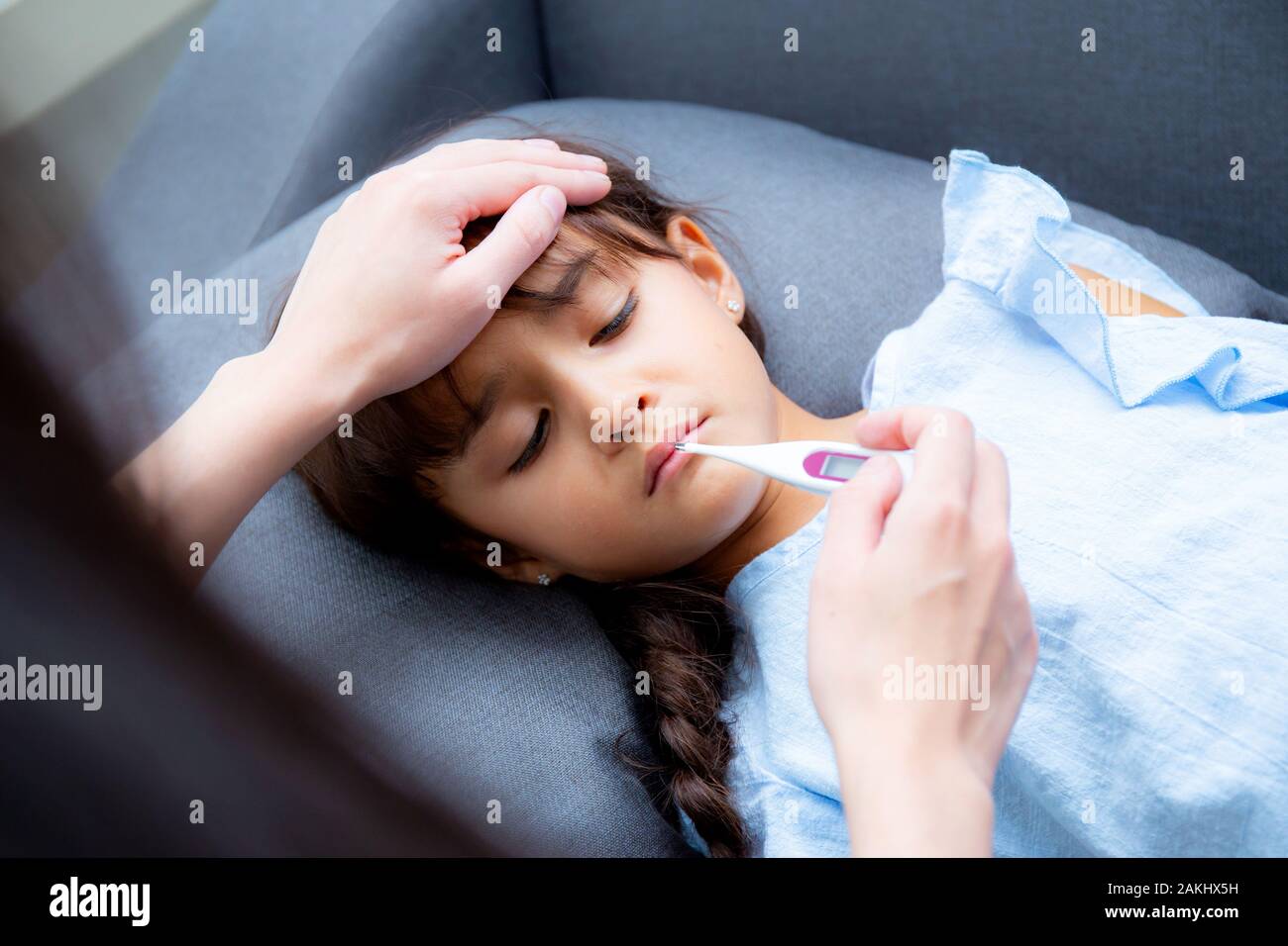 mother hand taking temperature with girl is a sick laying on sofa, Kid patient with mom check ...