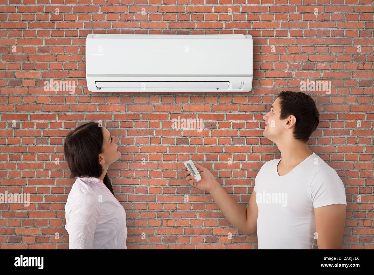 Young Couple Switching On The Air Conditioner With Remote Control ...