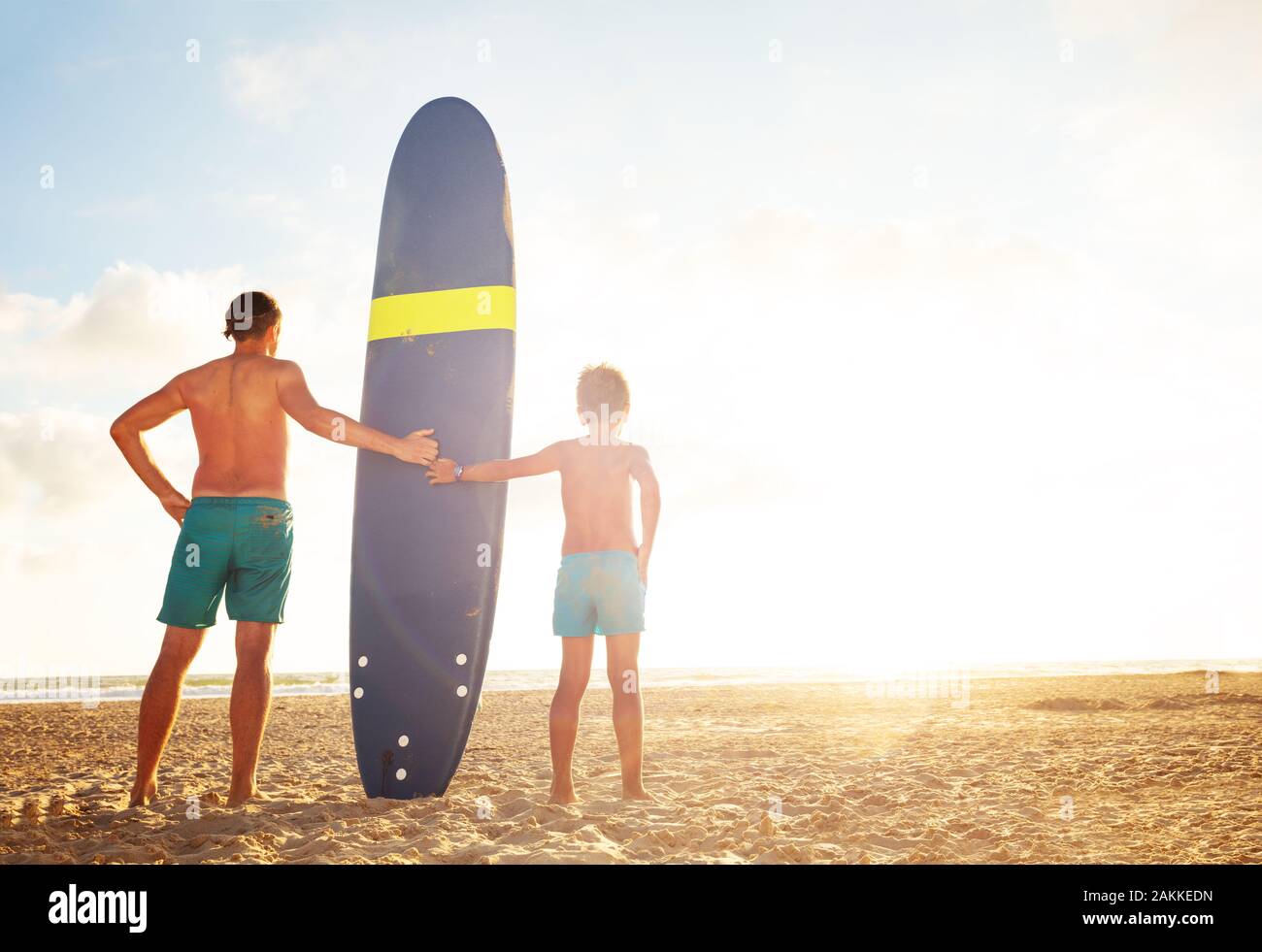 Father and son stand with surf board over sunset Stock Photo - Alamy