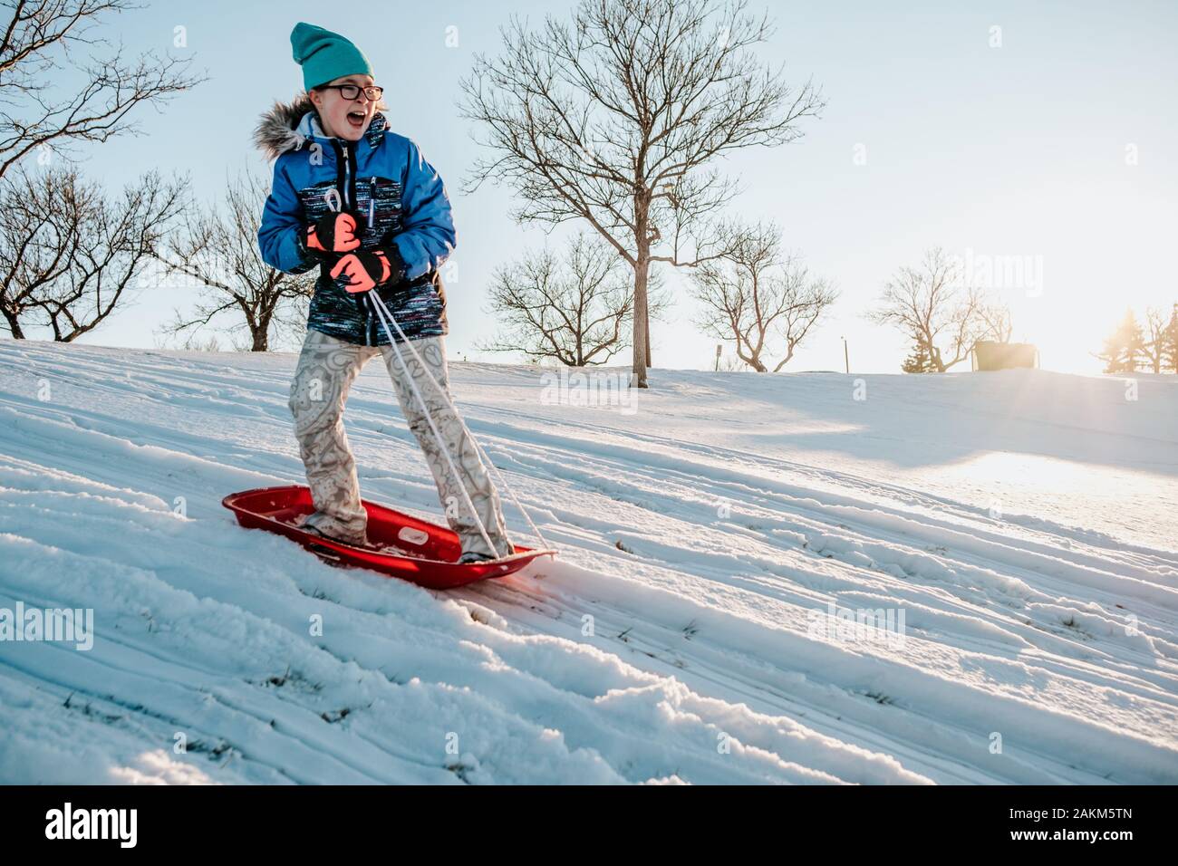 Action shot of girl standing on sled going down a hill in winter Stock ...