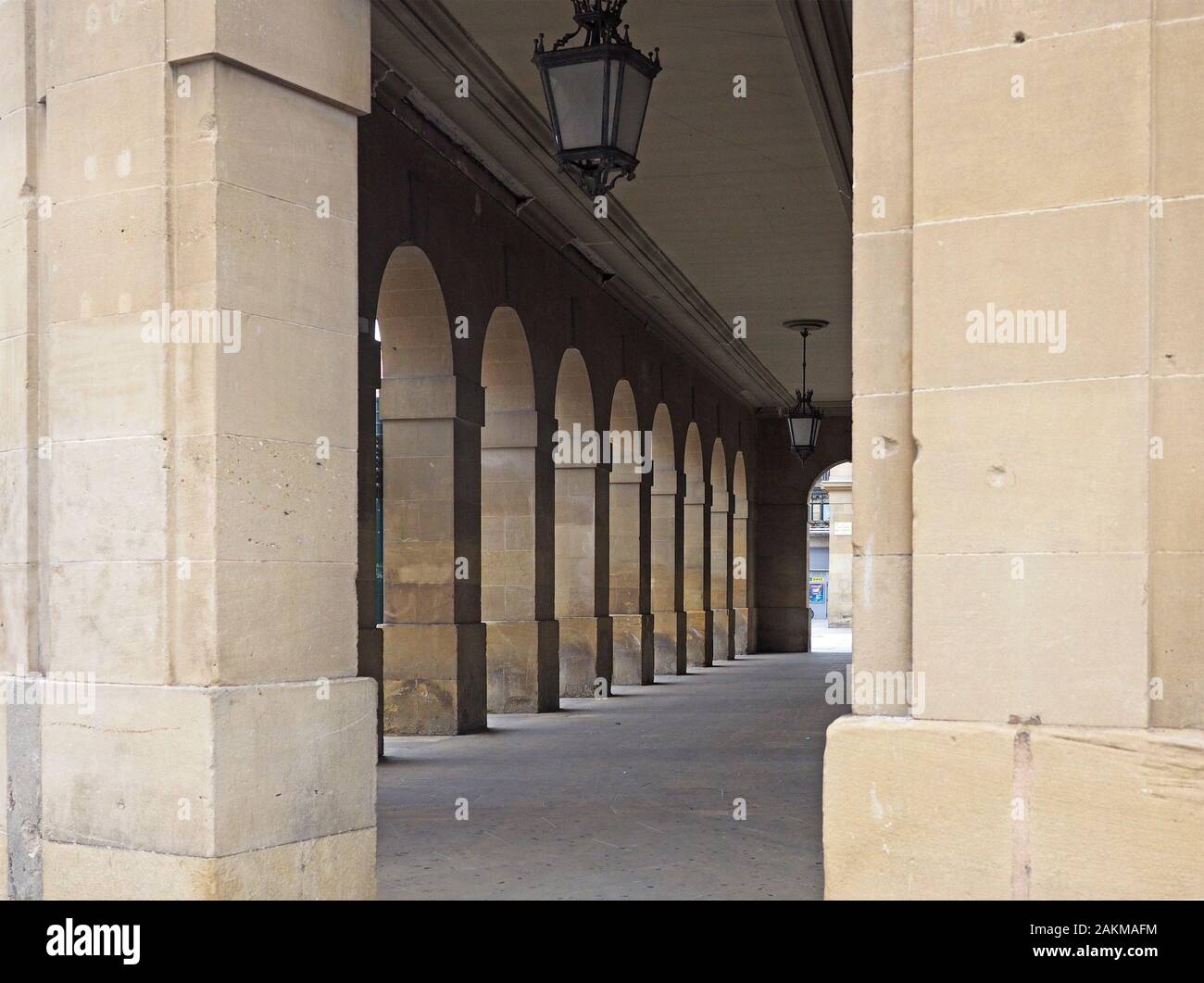 tall classical arches enclose a walkway along one side of a stone civic ...