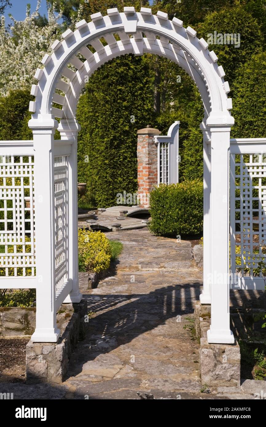 Flagstone path through white wooden arbour leading to formal garden ...