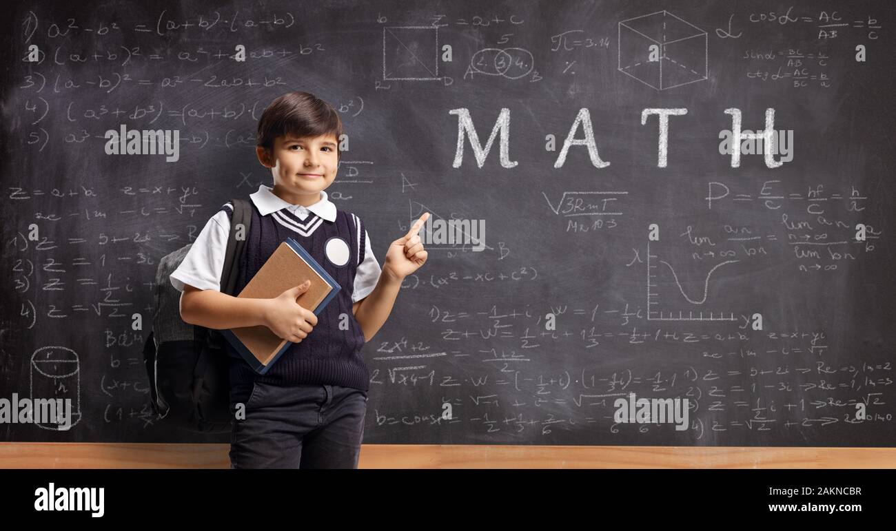 Schoolboy in a uniform holding books and pointing to a blackboard with ...
