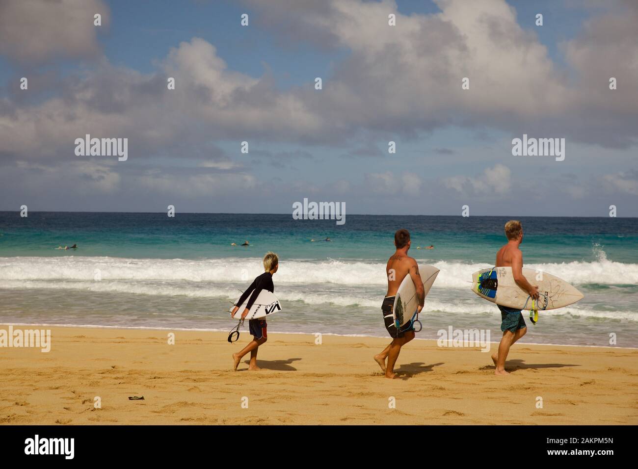 Three surfers walking on a beach Stock Photo - Alamy