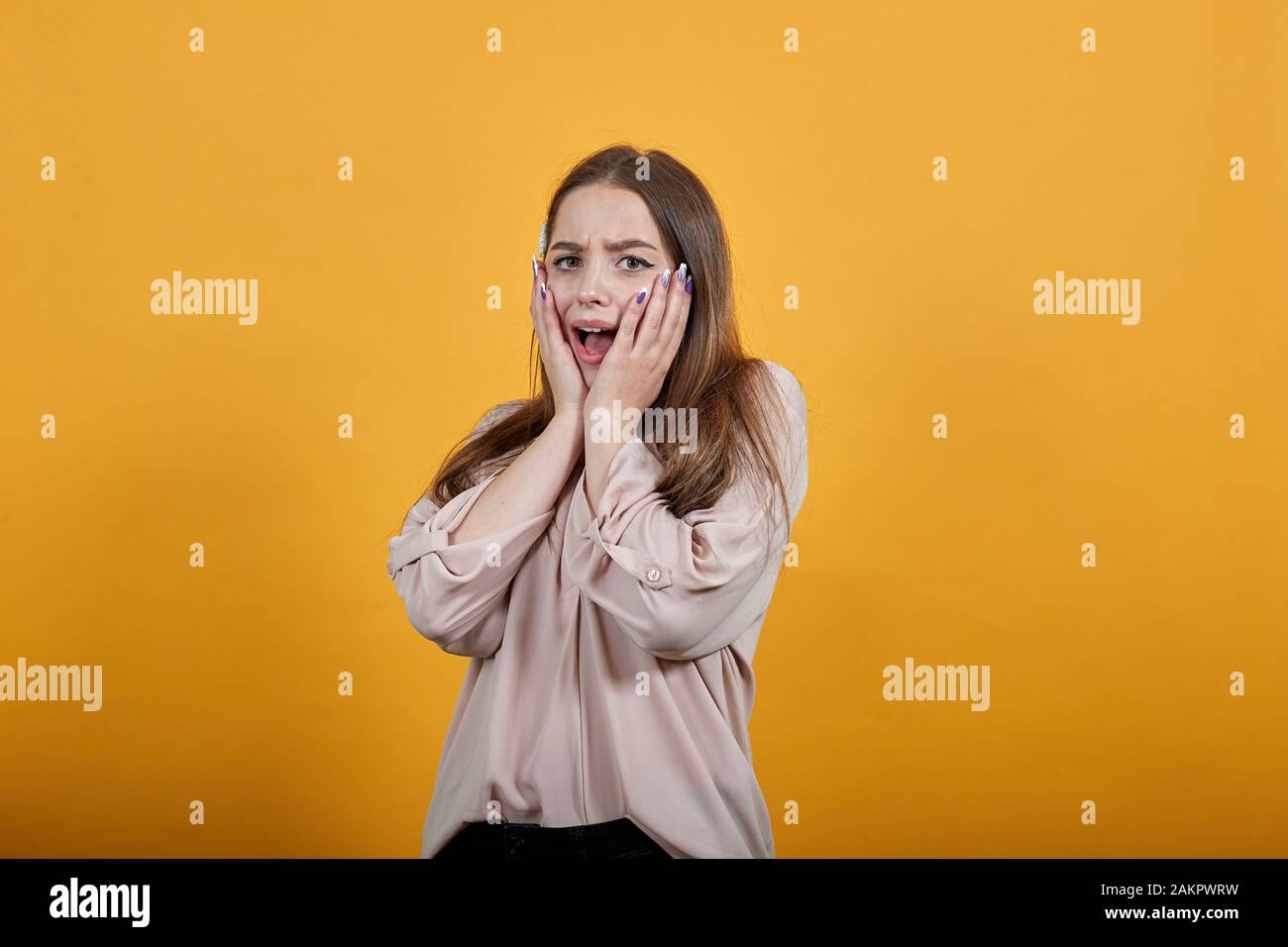 Surprised young caucasian woman keeping hands on cheeks, opened mouth ...
