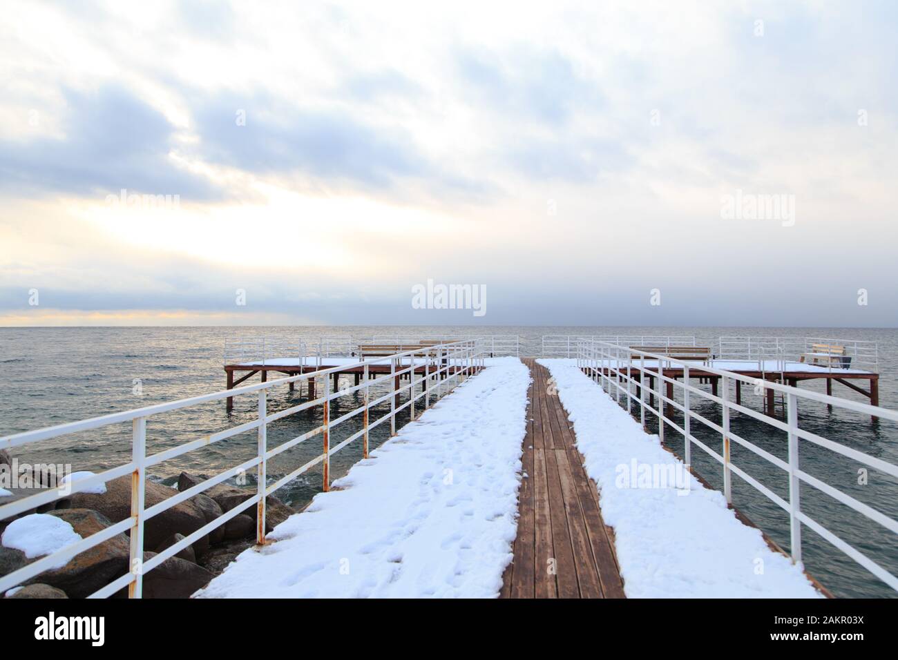Winter beach. Blue clear sea water, snow and a wooden pier. Skyline and ...