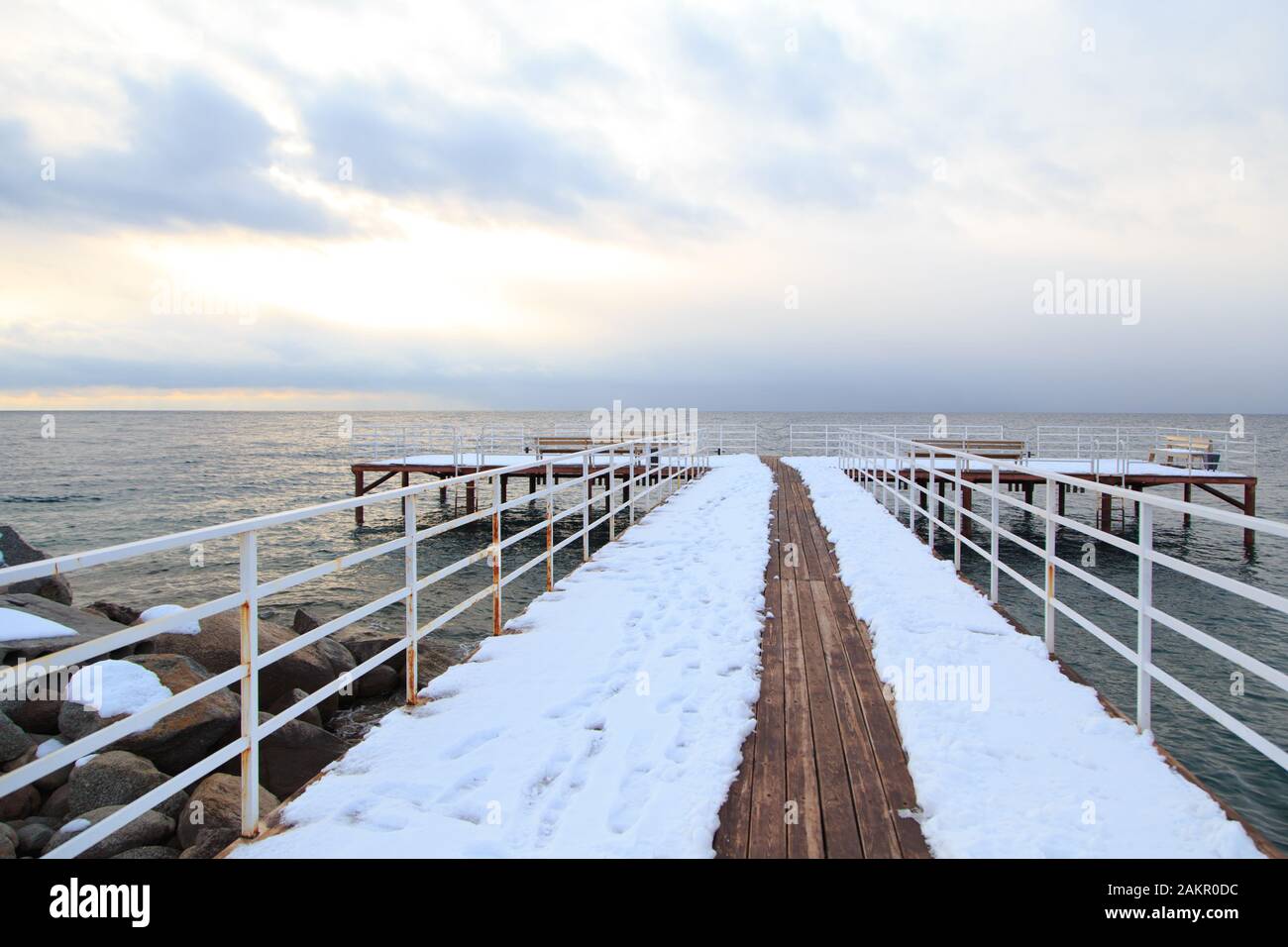 Winter beach. Blue clear sea water, snow and a wooden pier. Skyline and ...