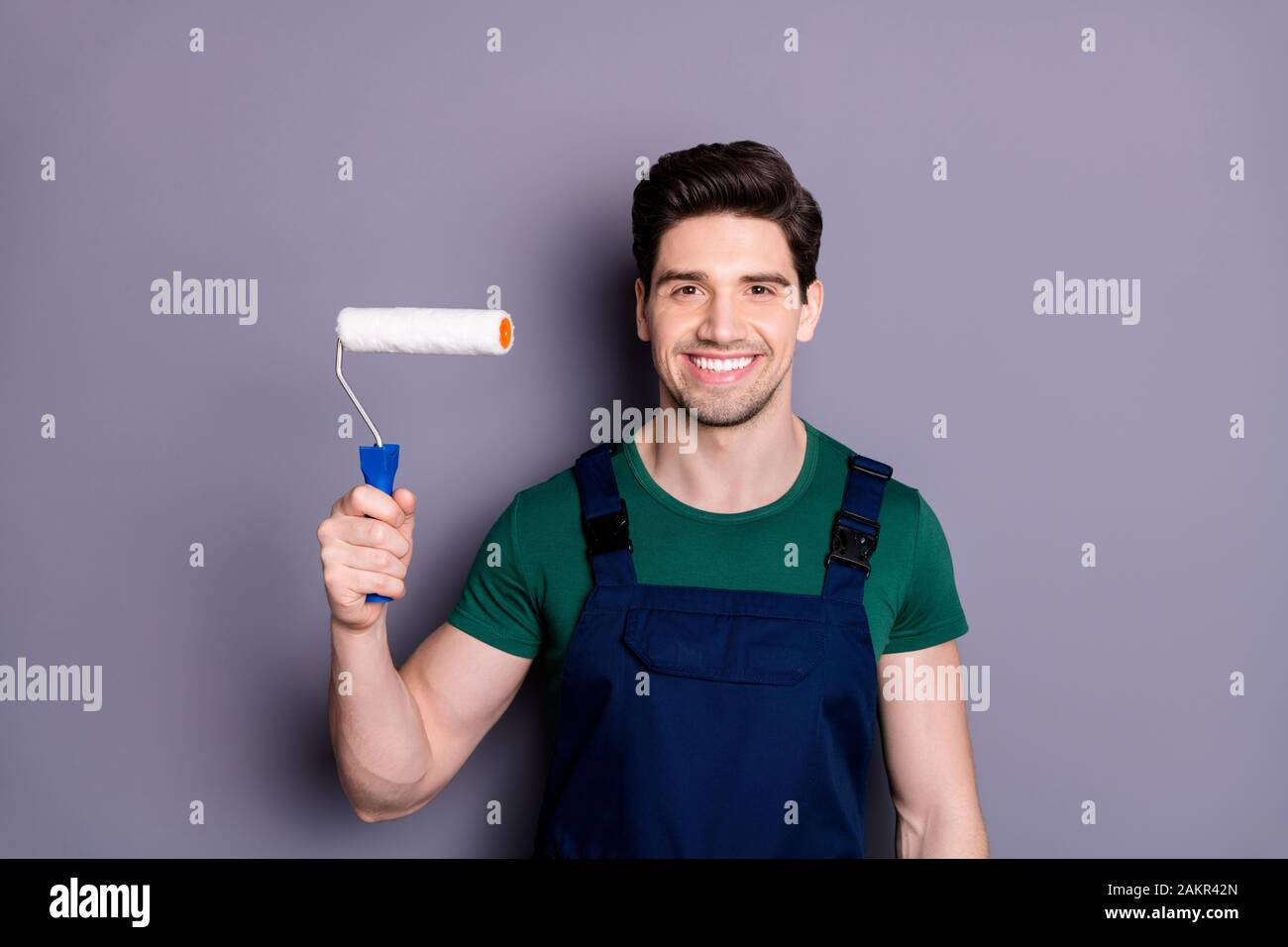 Portrait of positive cheerful house painter man hold white roller ready ...