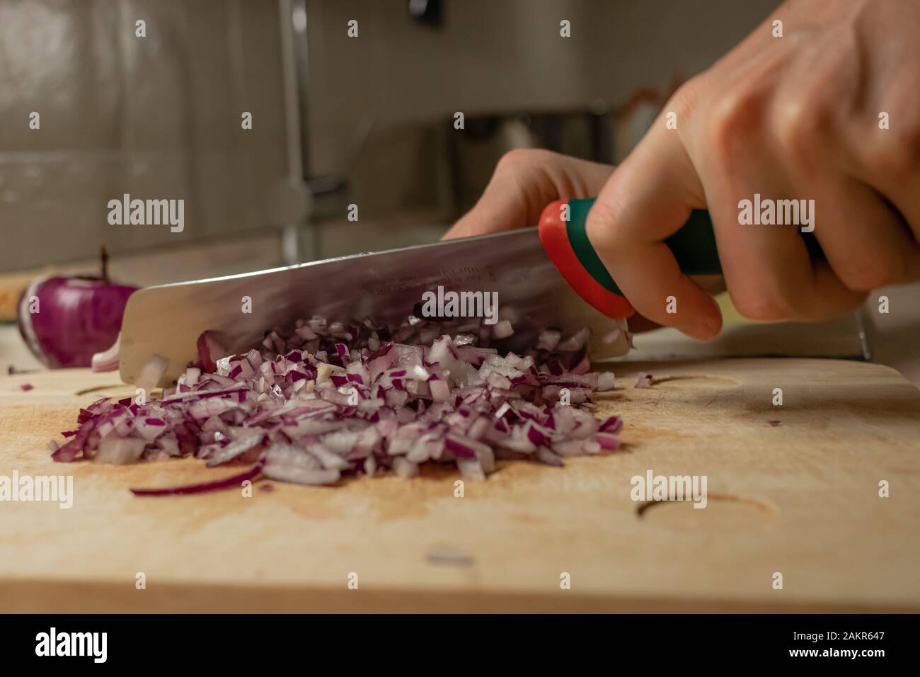 close up of a knife chopping red onions on a chopping board in the kitchen with artificial light ...