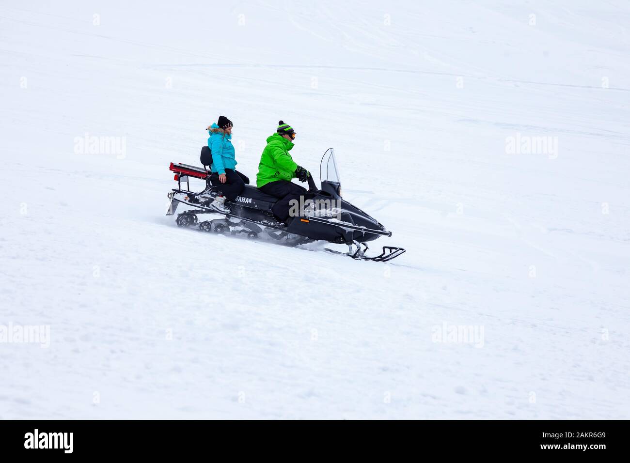 Altai, Russia - 01.01.2020: People on a snowmobile rises uphill over ...