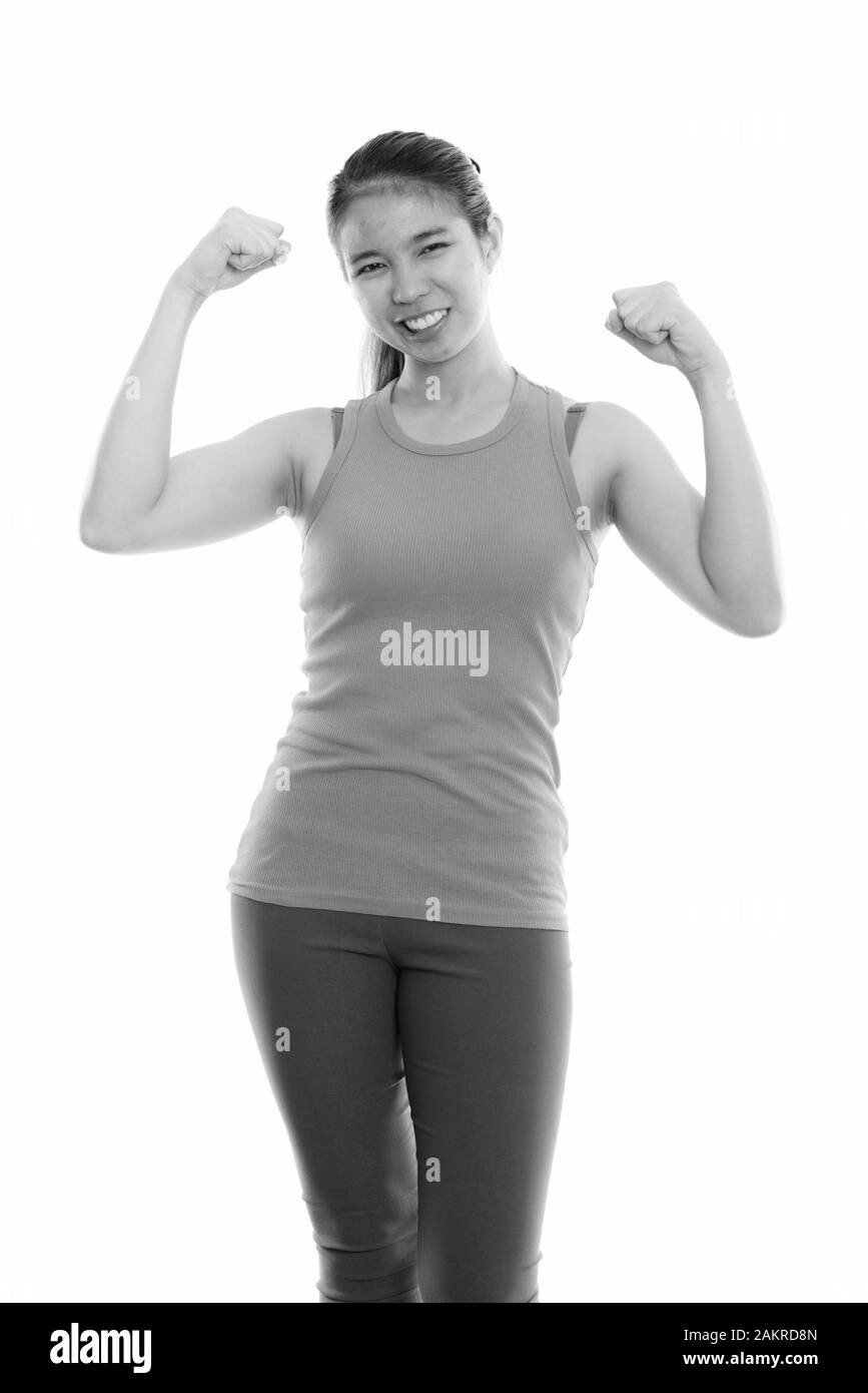 Studio shot of young happy Asian woman smiling while flexing both arms ...