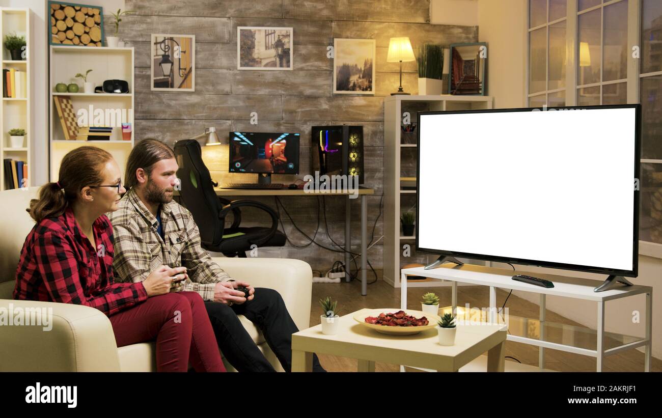 Cheerful couple sitting on couch playing video games on tv with green ...