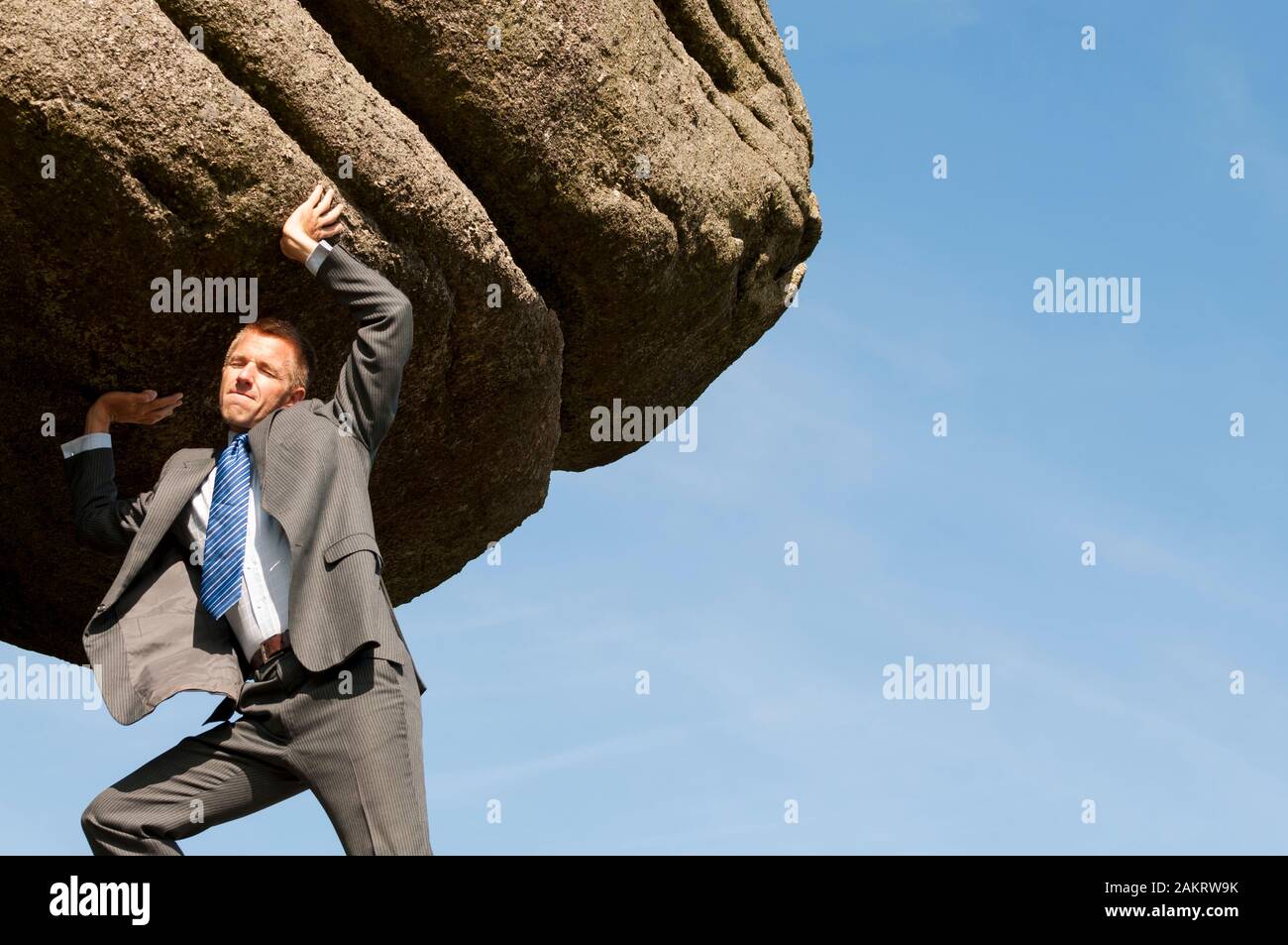 Strong businessman struggling to lift massive boulder into blue sky ...