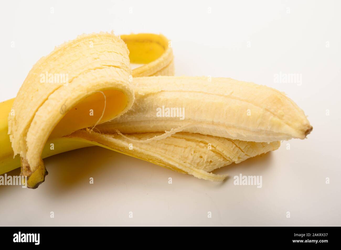 One ripe yellow partially peeled banana on a white background. Close up ...