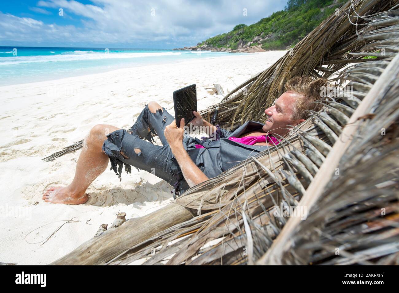 Castaway businessman lying back in a makeshift beach hut shelter ...