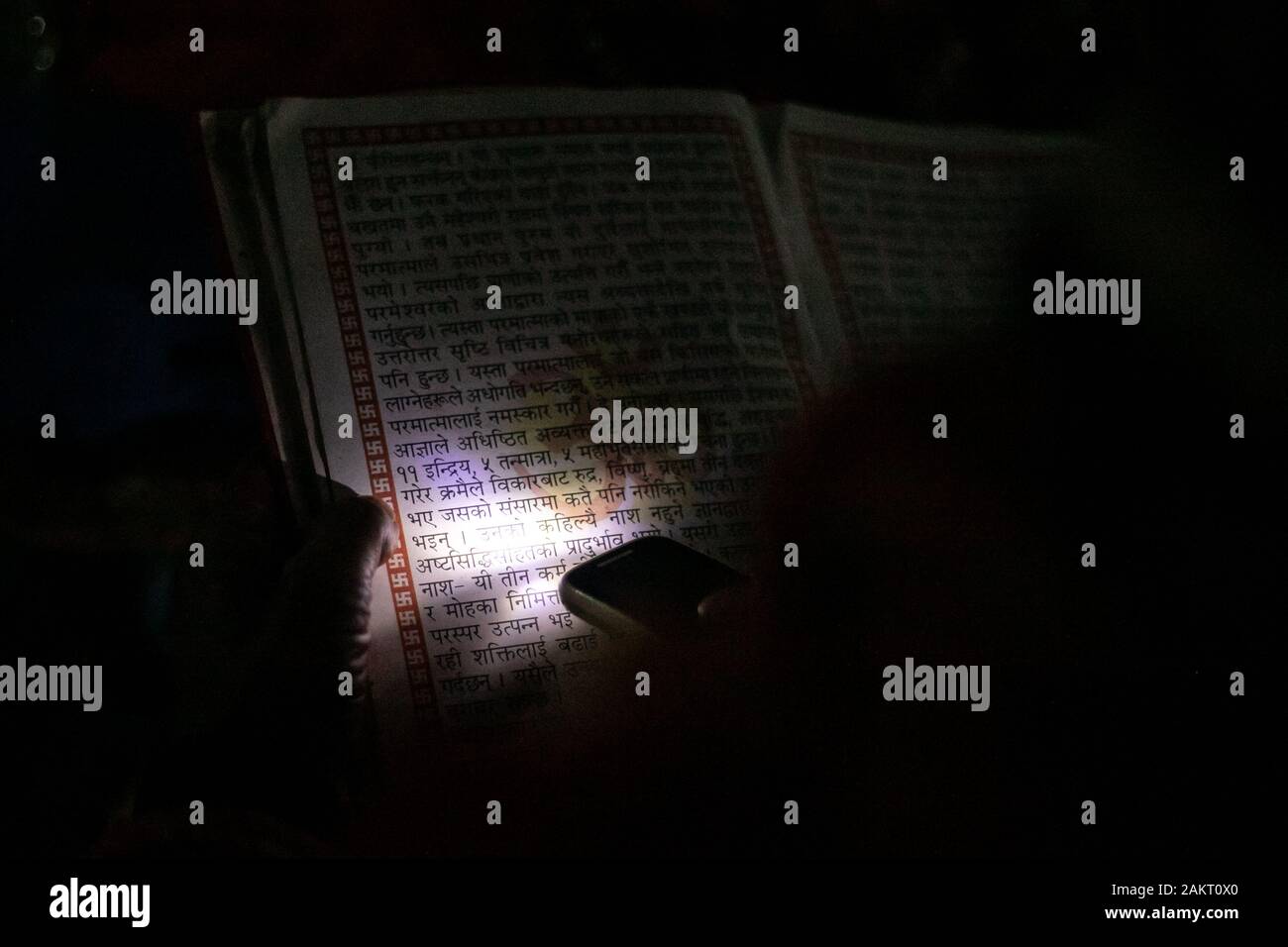 A priest reads a religious script (swasthani barta Katha book) using a ...